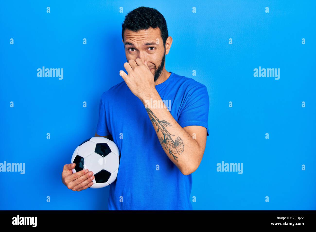 Hispanic man with beard holding soccer ball smelling something stinky ...