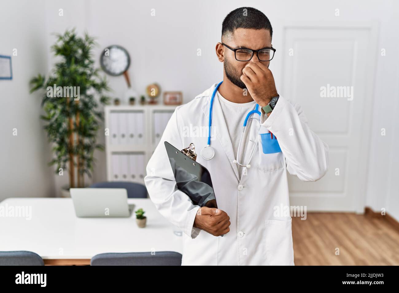 Young indian man wearing doctor uniform and stethoscope smelling ...