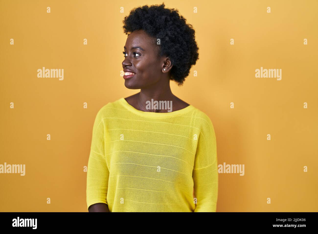 African young woman standing over yellow studio looking away to side ...