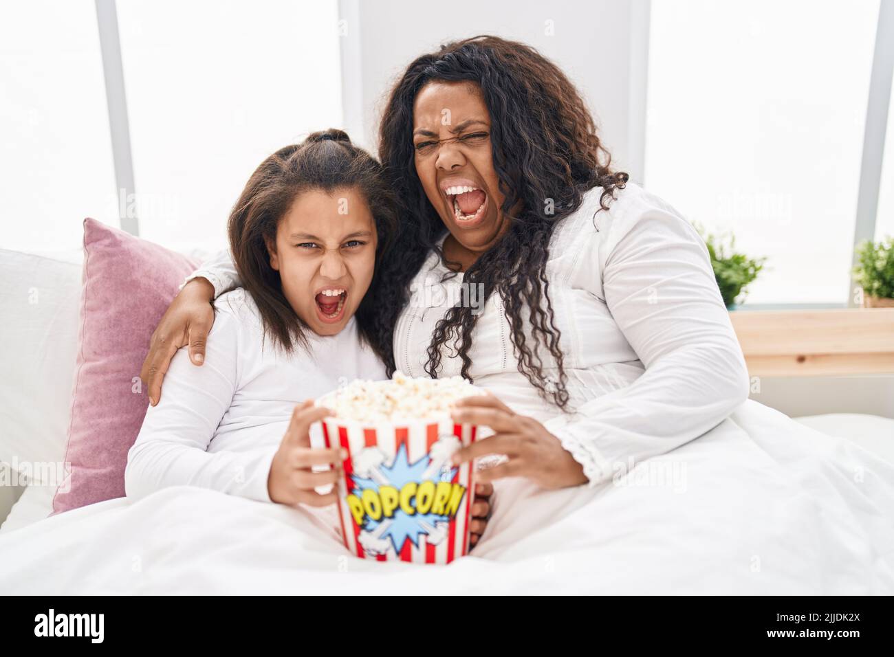 Mother and young daughter eating popcorn in the bed angry and mad ...