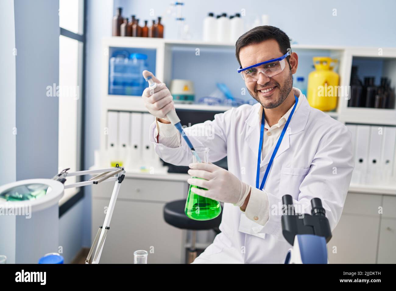 Young hispanic man scientist measuring liquid using pipette at ...