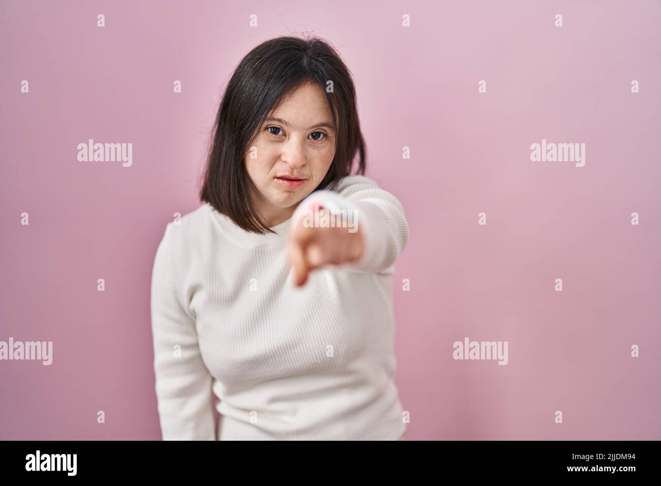 Woman with down syndrome standing over pink background pointing ...
