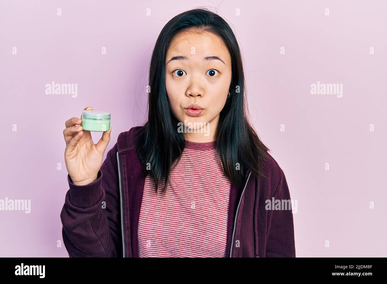 Young chinese girl holding cosmetic moisturizer facial cream scared and ...