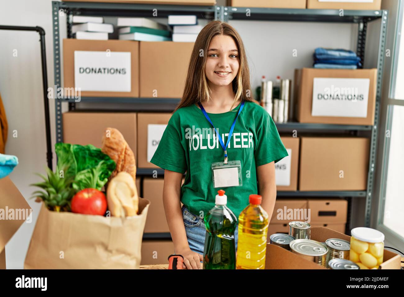 Adorable girl wearing volunteer uniform standing at charity center ...