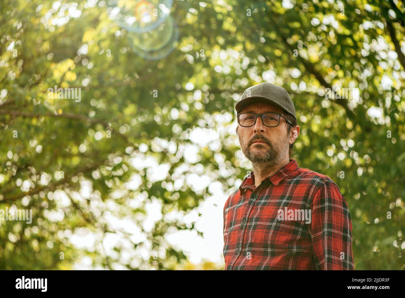 Portrait of male farmer wearing plaid shirt and trucker's hat posing in ...