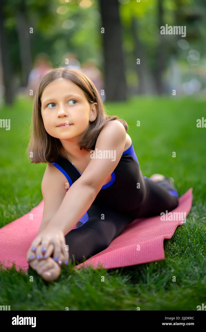 a little girl in the park is doing yoga stretching leaning on her leg ...