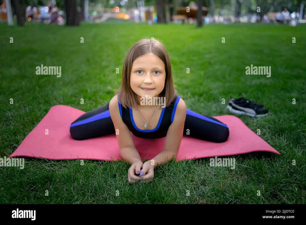 in the park, a little girl performs a frog element, doing stretching on ...