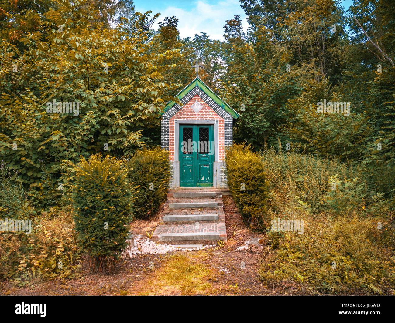 A historical small chapel with its green door and roof, red and blue ...