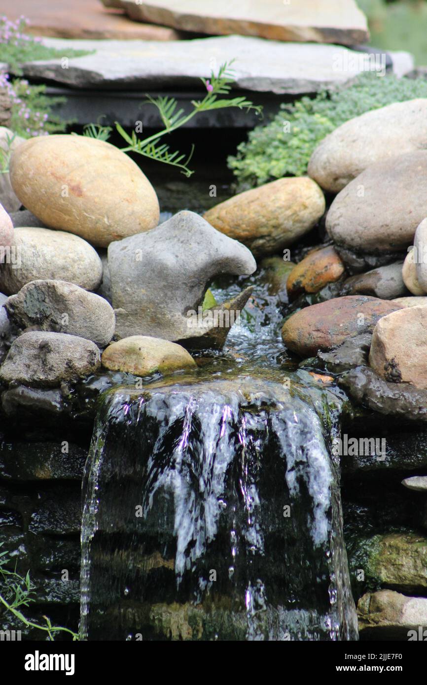 A vertical shot of a small waterfall with different types of stones ...