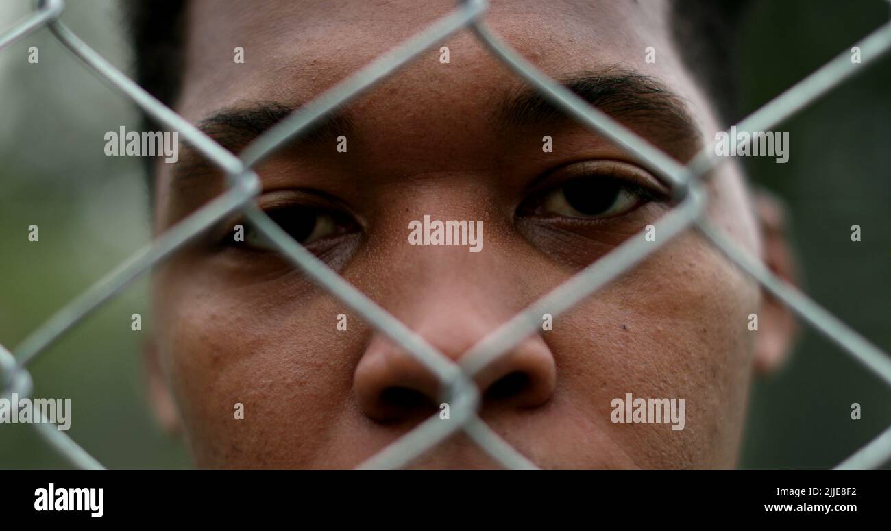 Serious African black man behind metal fence, close-up eyes staring ...