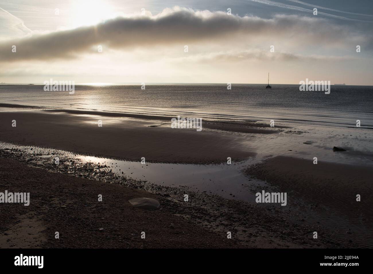 A calm beach view with a sole boat in the sea under a cloudy sky ...