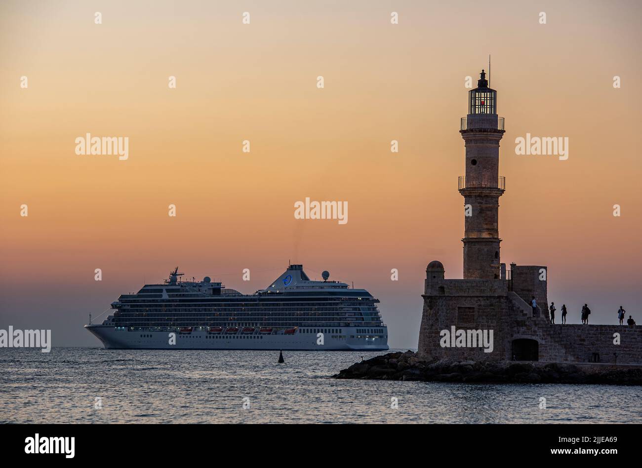 cruise liner passing the historic lighthouse at sunset at the harbour ...