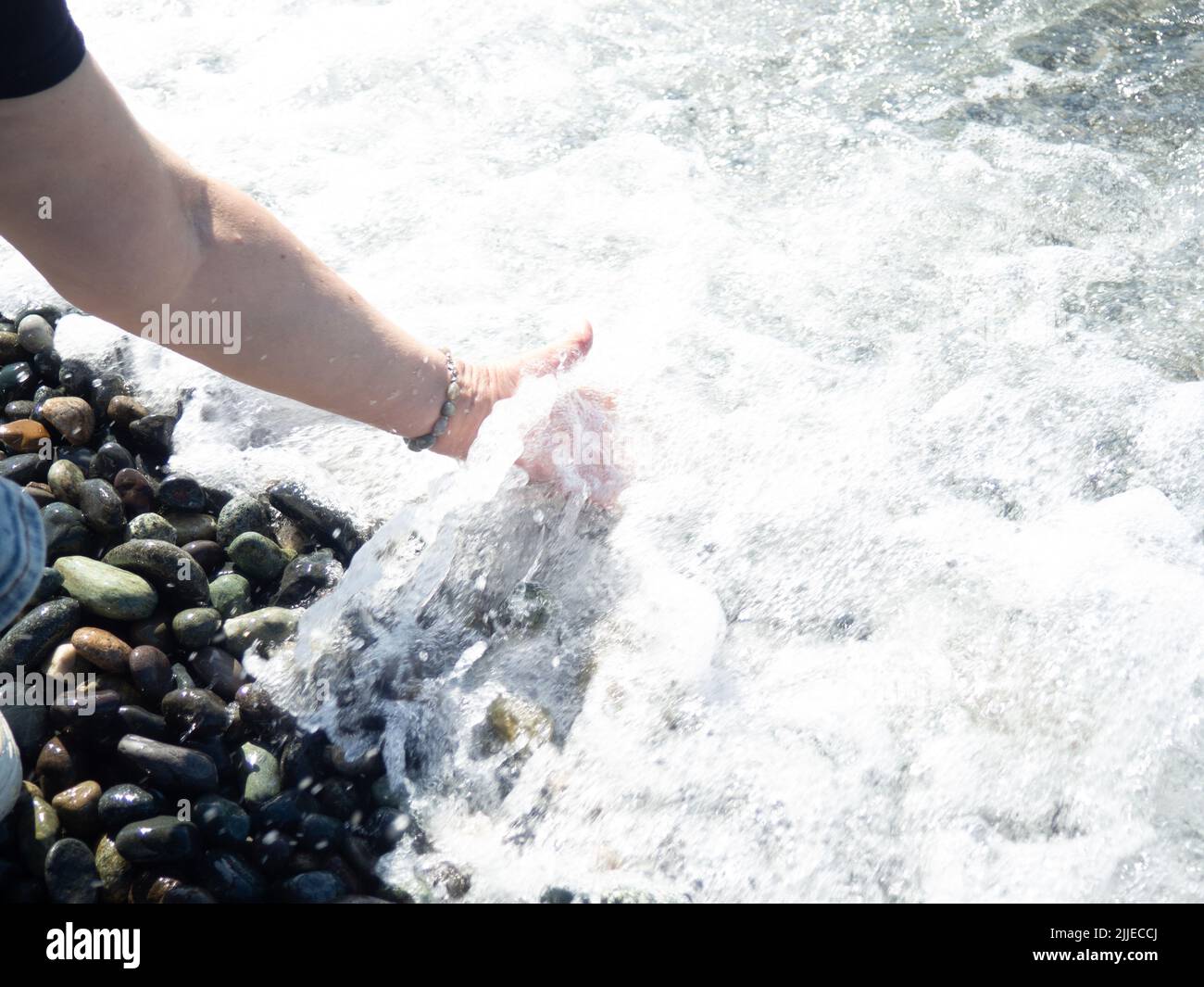 A hand with a bracelet made of stones reaches for the water. Sea wave ...