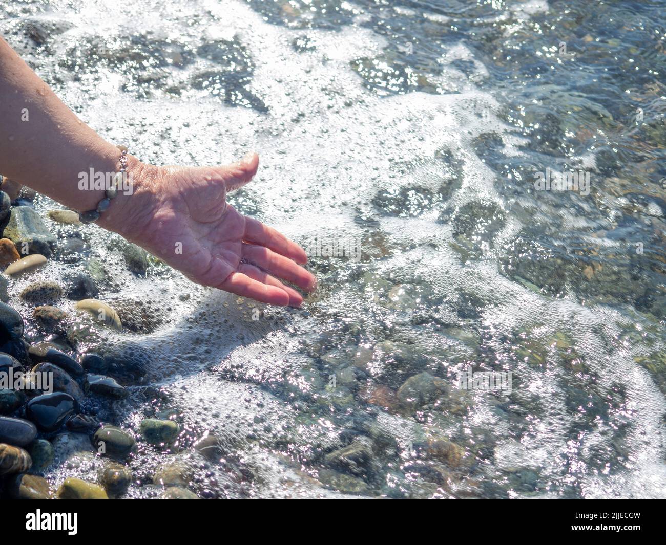 A hand with a bracelet made of stones reaches for the water. Sea wave ...