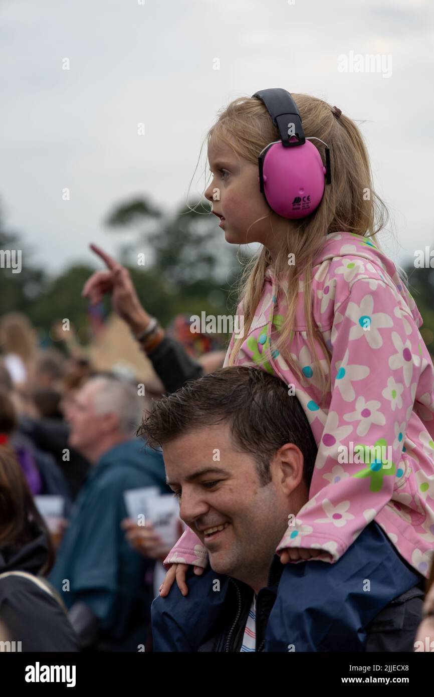 young girl with ear defenders on dads shoulders inFestival crowd at ...