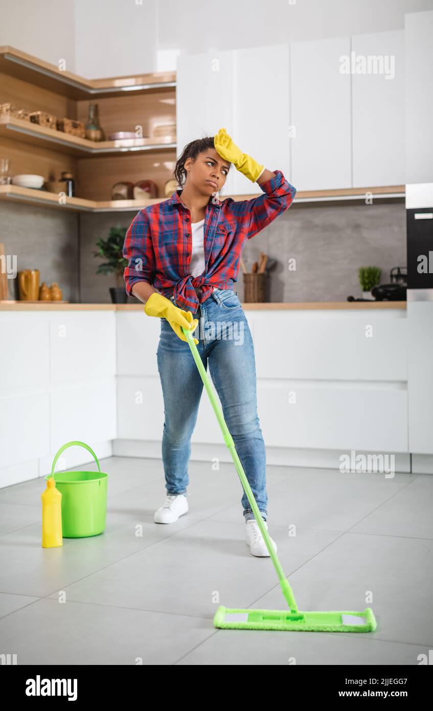 Tired sad young black lady housewife in rubber gloves with mop washes ...