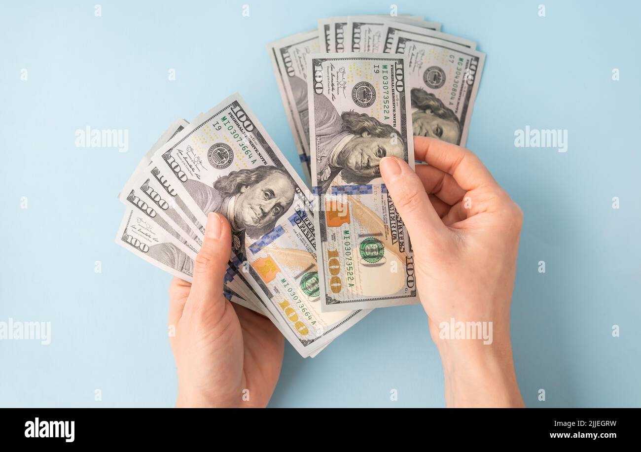 Female hands counting 100 dollar bills isolated on a blue background ...