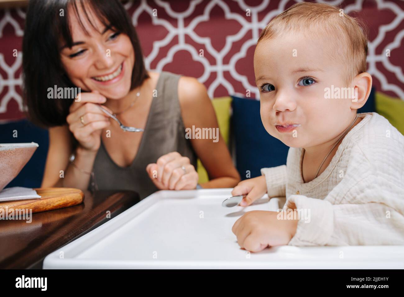 Mischievous perky smiling infant baby smiling with his mouth full. While being spoon fed by his ...