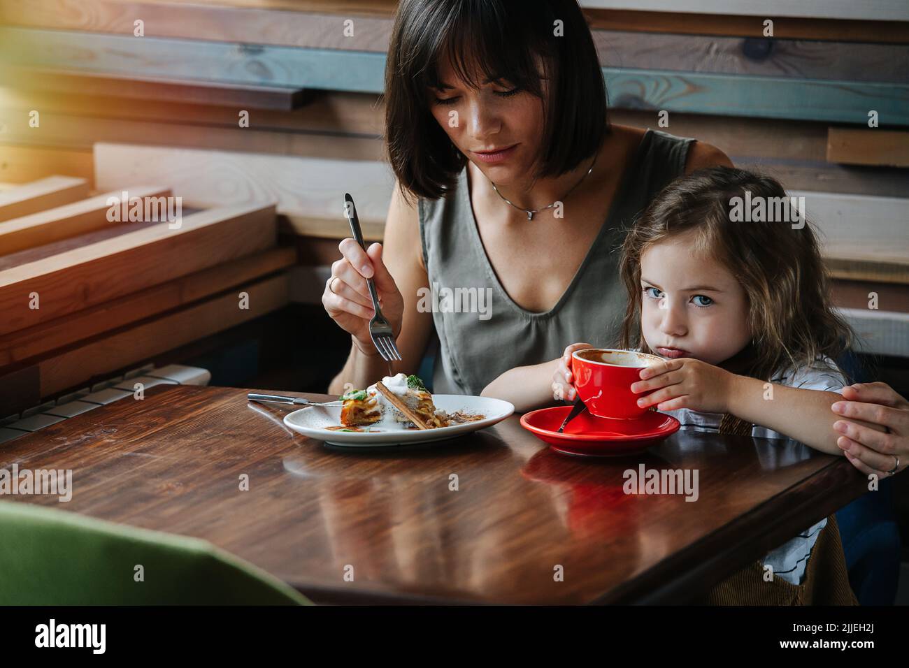 Mom is sitting in a cafe with her ten year old daughter, she is eating ...