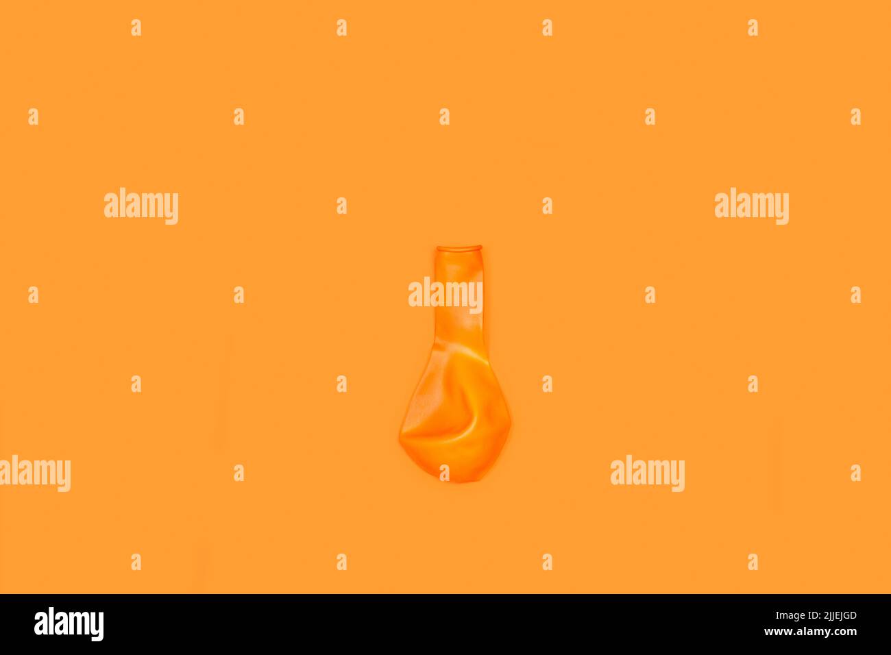 A deflated orange pink balloon on an orange background with copy space ...