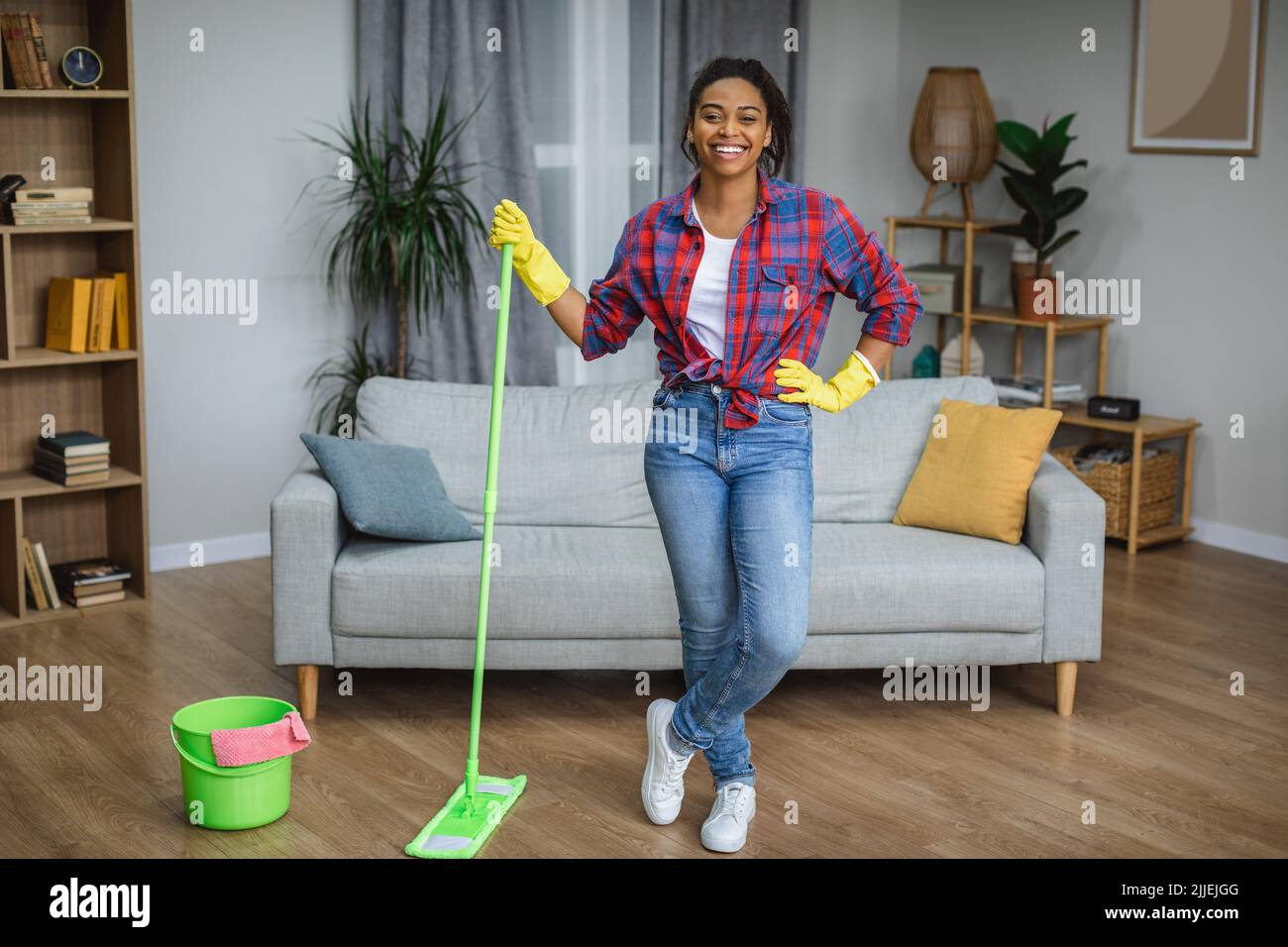 Happy young african american woman housewife with mop cleaning floor in ...