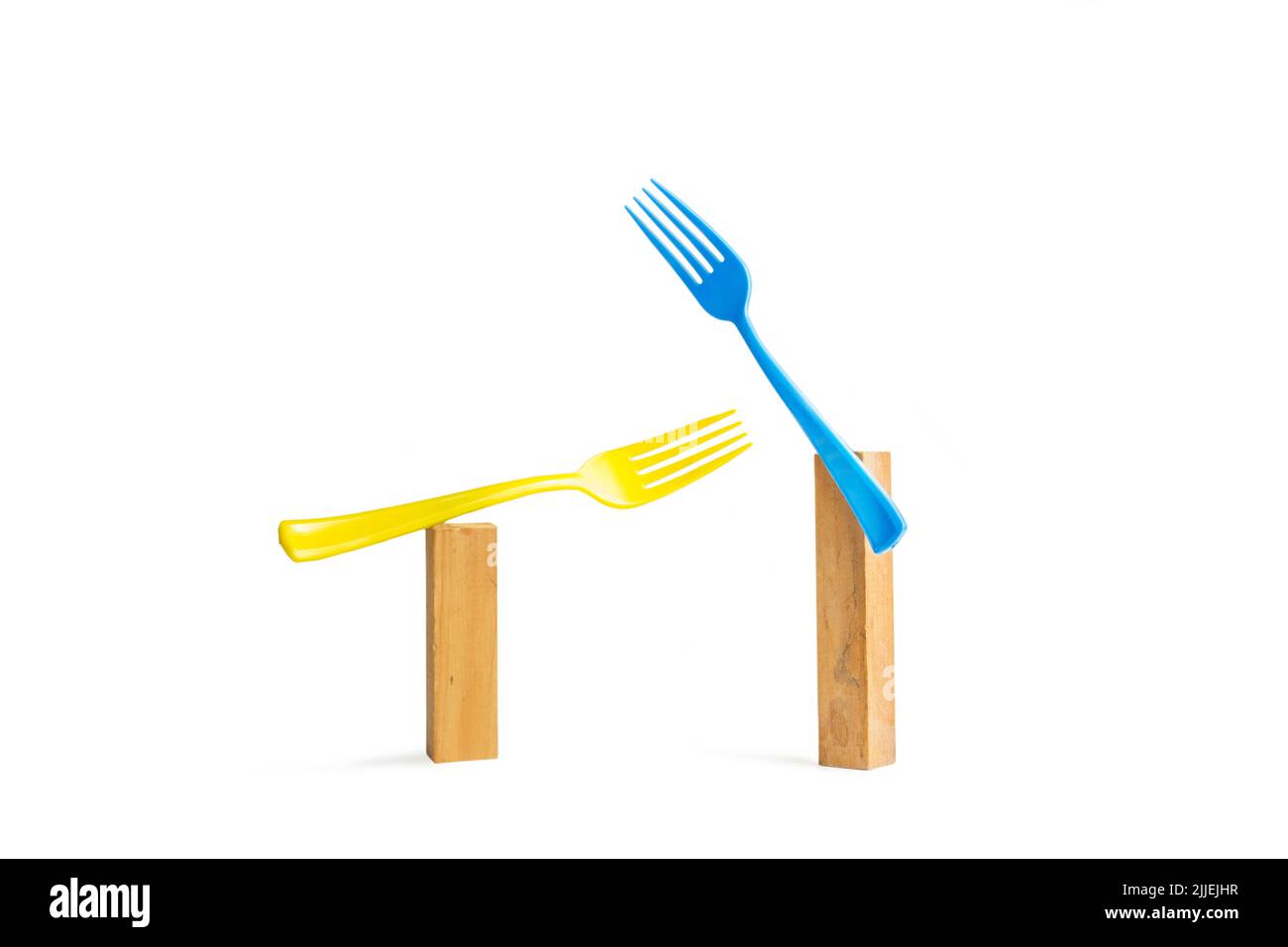 Blue and yellow plastic forks on wooden bricks on a white background ...