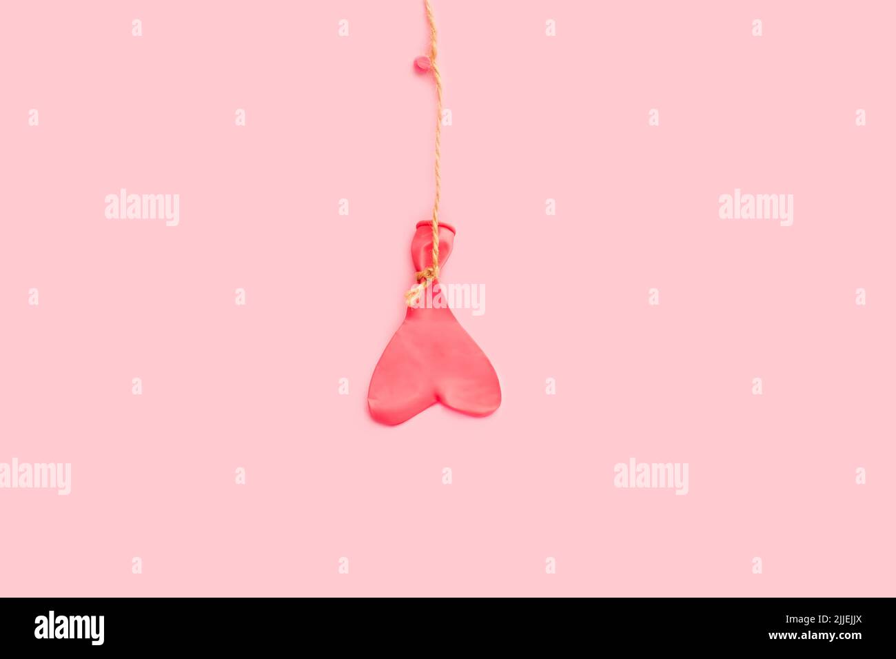 A heart shape deflated pink balloon hanging from a sisal thread on a ...
