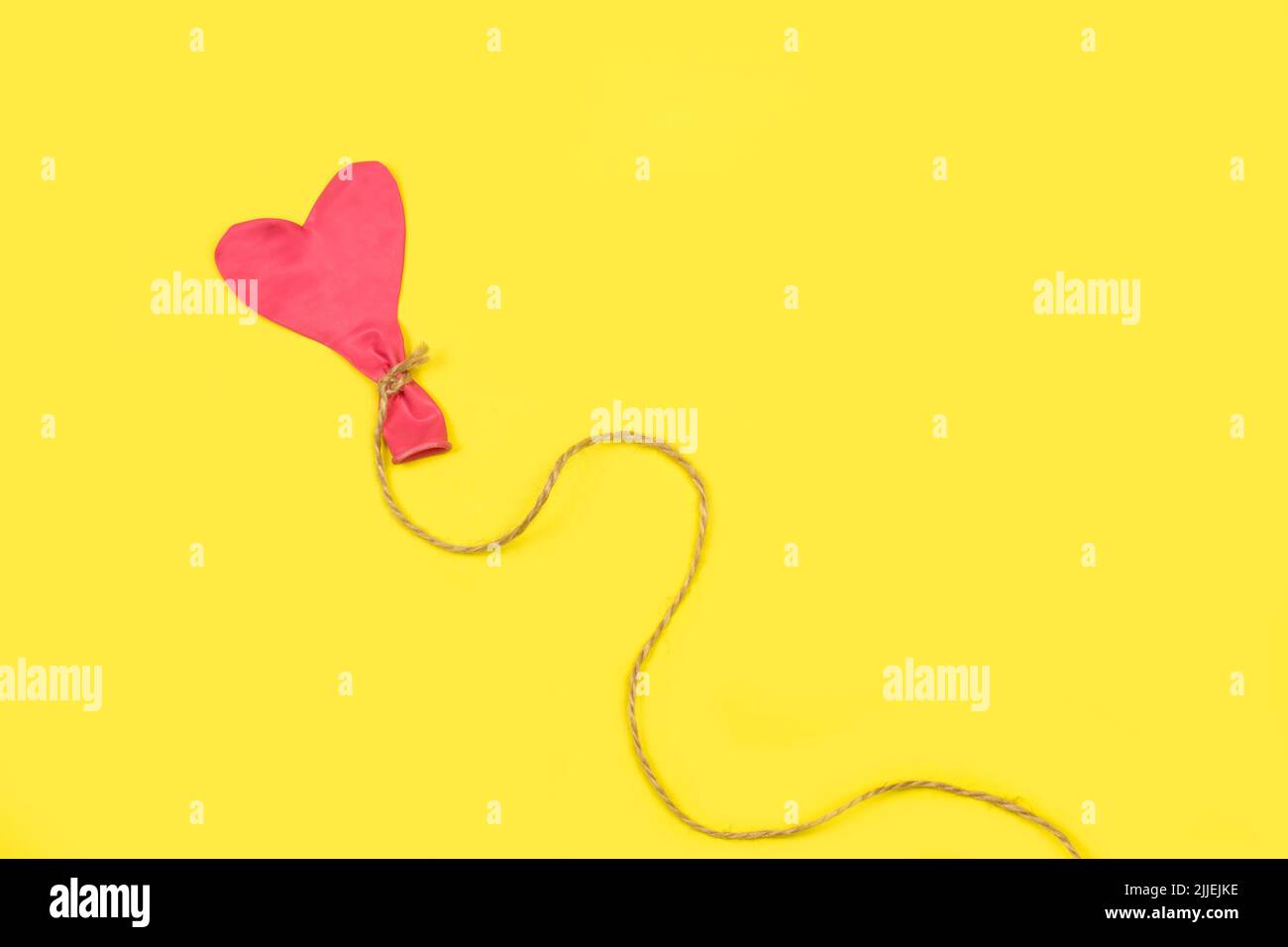 A heart shape deflated pink balloon tied with a sisal yarn on a yellow ...
