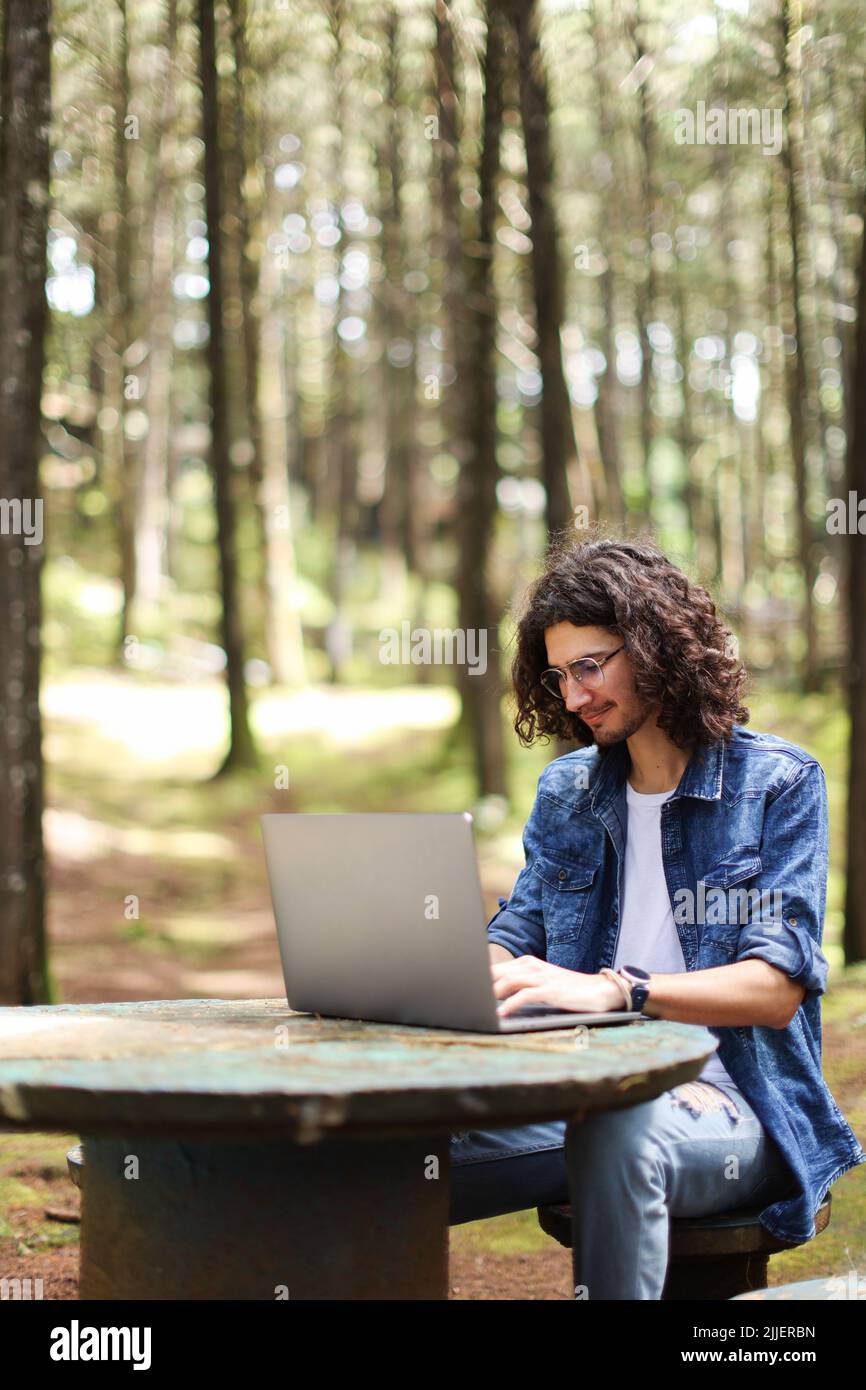 Young latin man sitting in the forest working with laptop freelancing ...