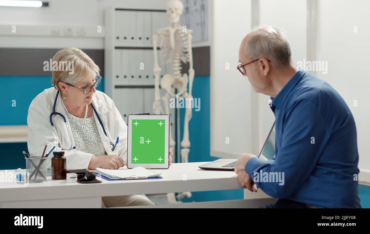 General practitioner vertically holding tablet with greenscreen on ...