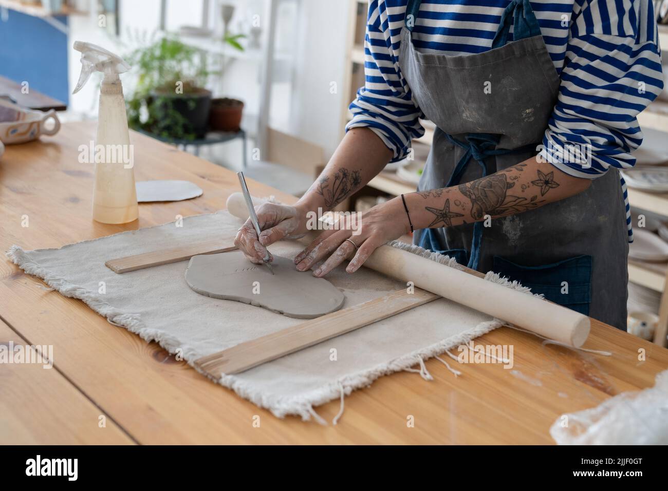 Craft artist making object out of clay in studio, using fettling knife ...