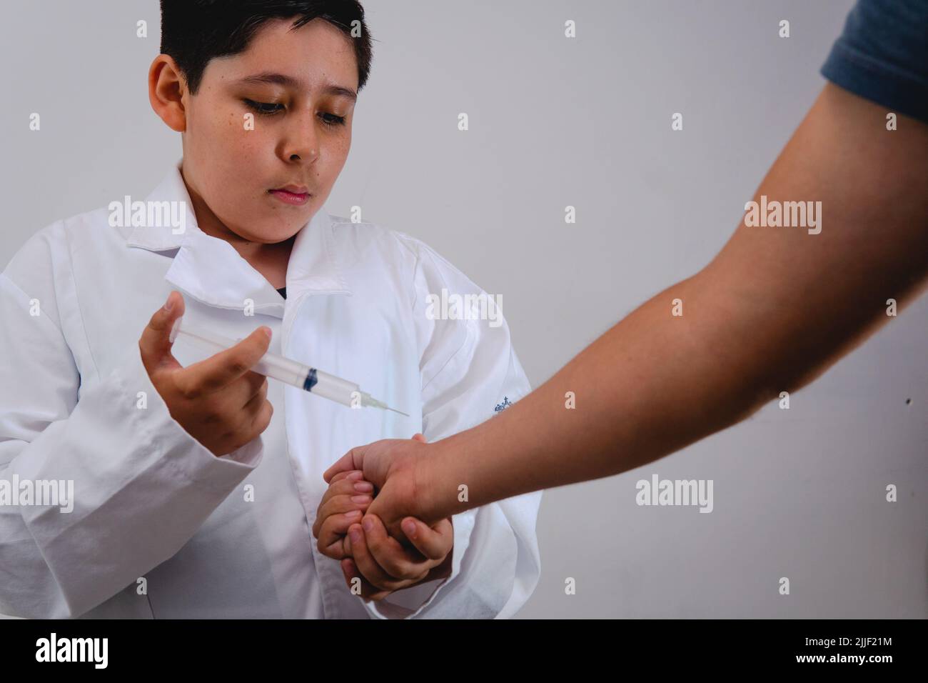 A boy disguised as a doctor in a large white coat with a needle about ...