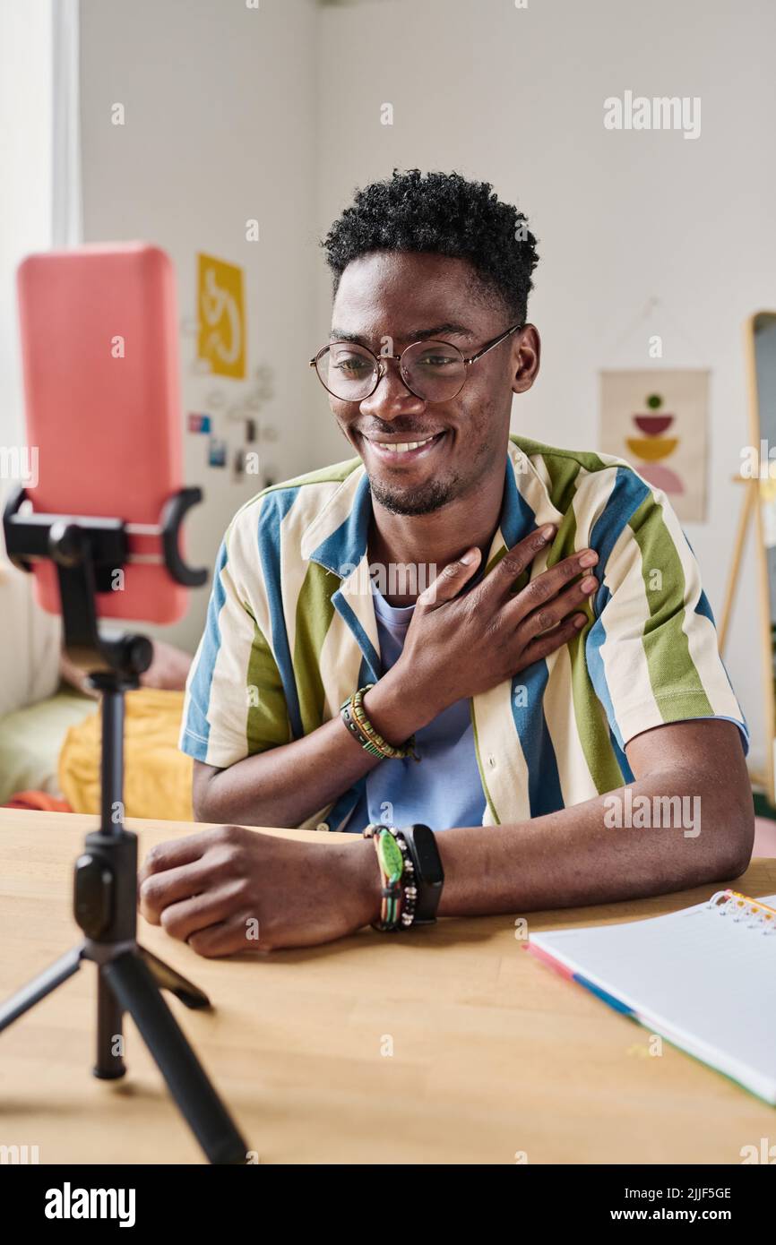 African teenage boy smiling at camera of his smartphone on tripod while ...
