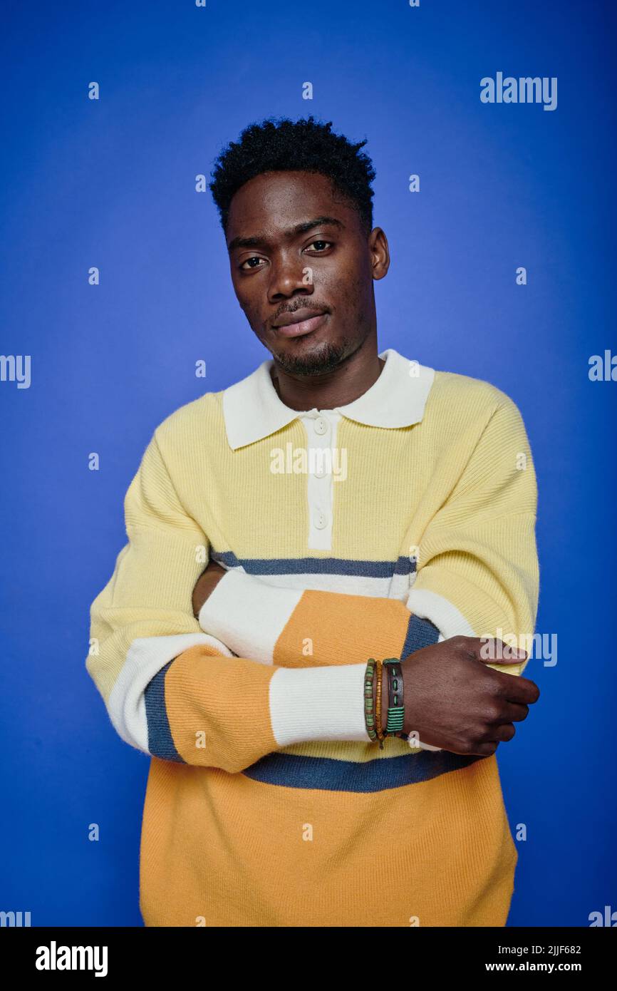 Portrait of African teenage boy standing with his arms crossed and looking at camera against ...