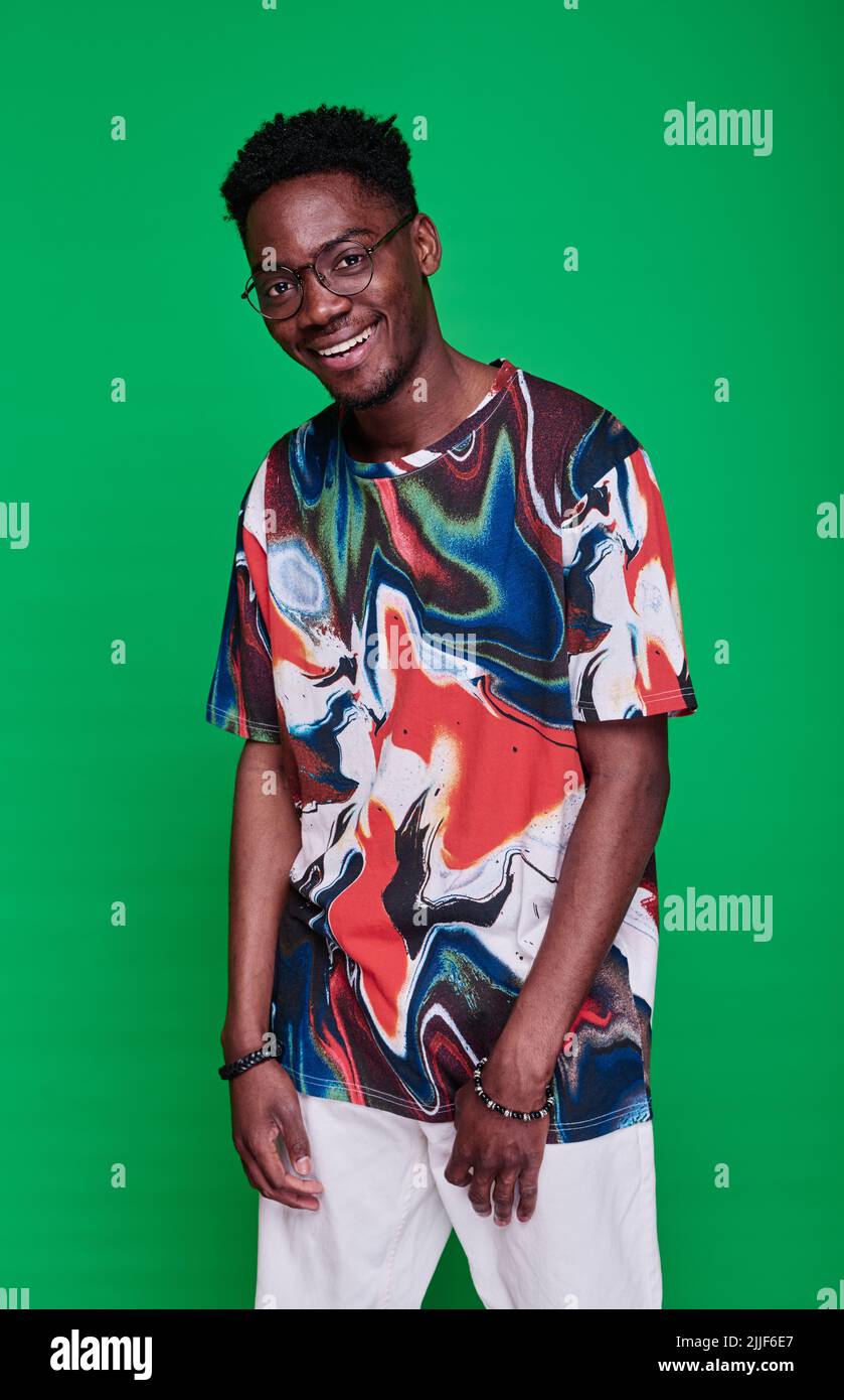 Portrait of African teenage boy in bright shirt smiling at camera posing against green ...