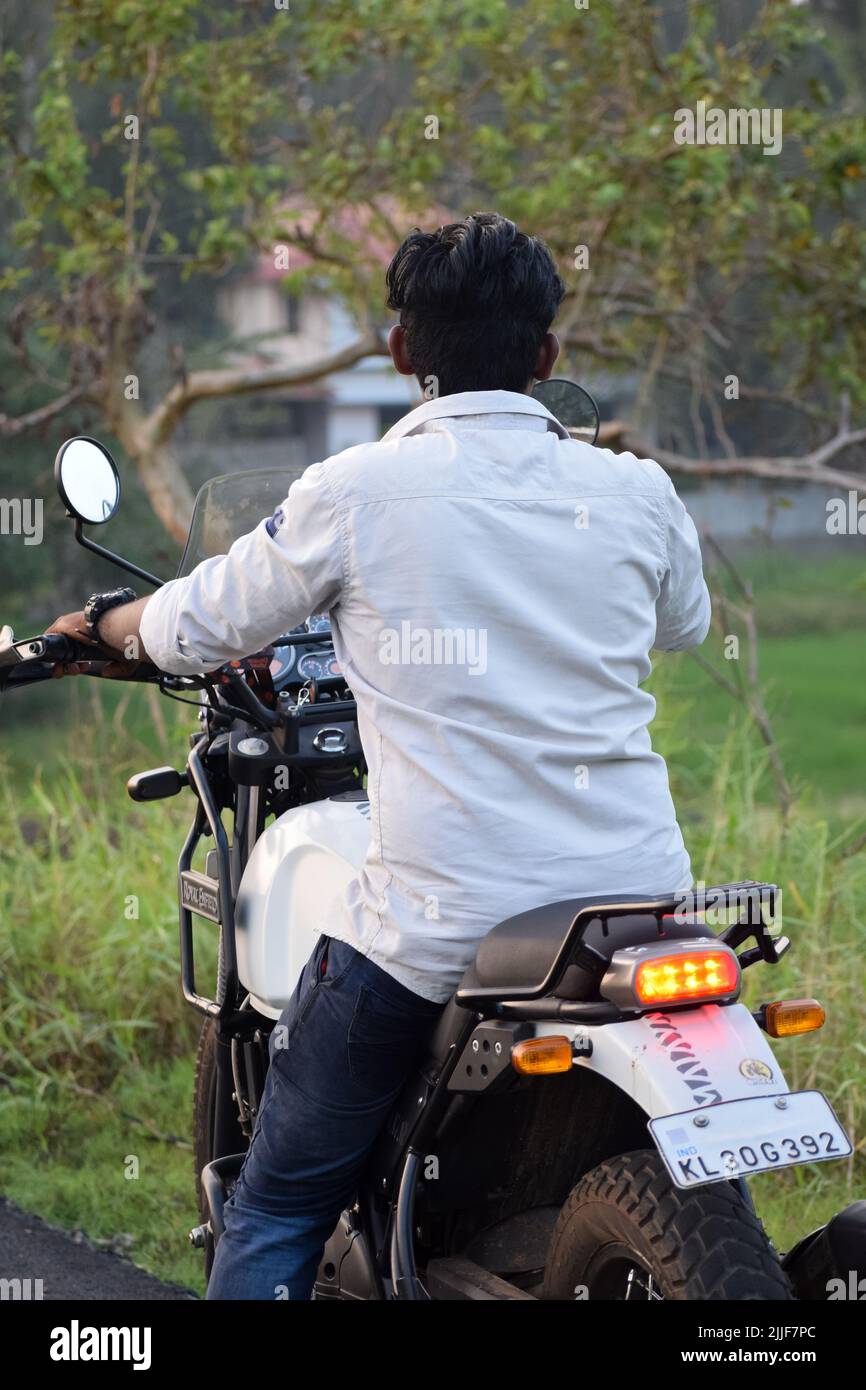 Rear view of an indian young man riding a motorcycle near a paddy field ...