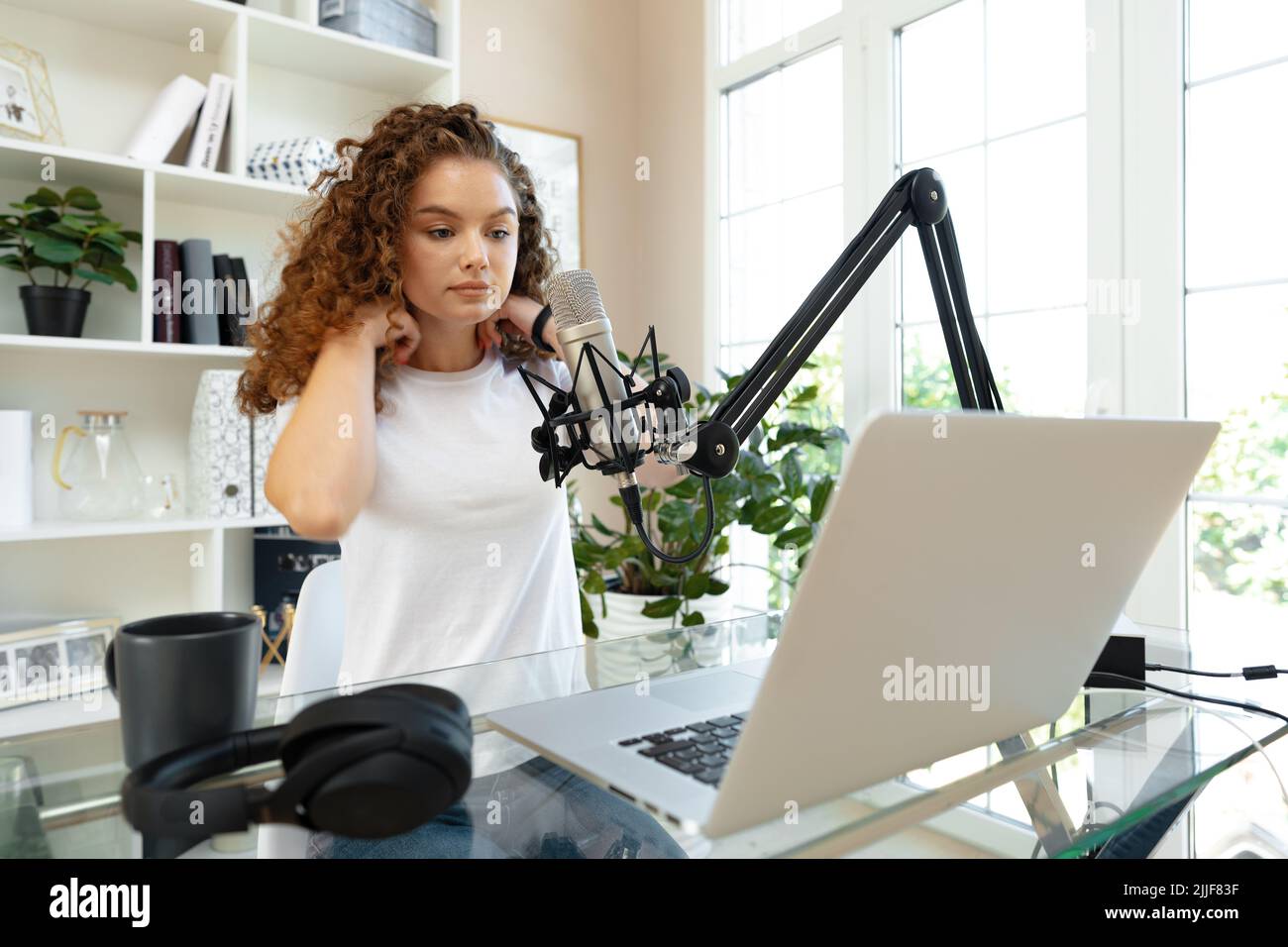 Woman vlogger looking at laptop and recording video with microphone ...