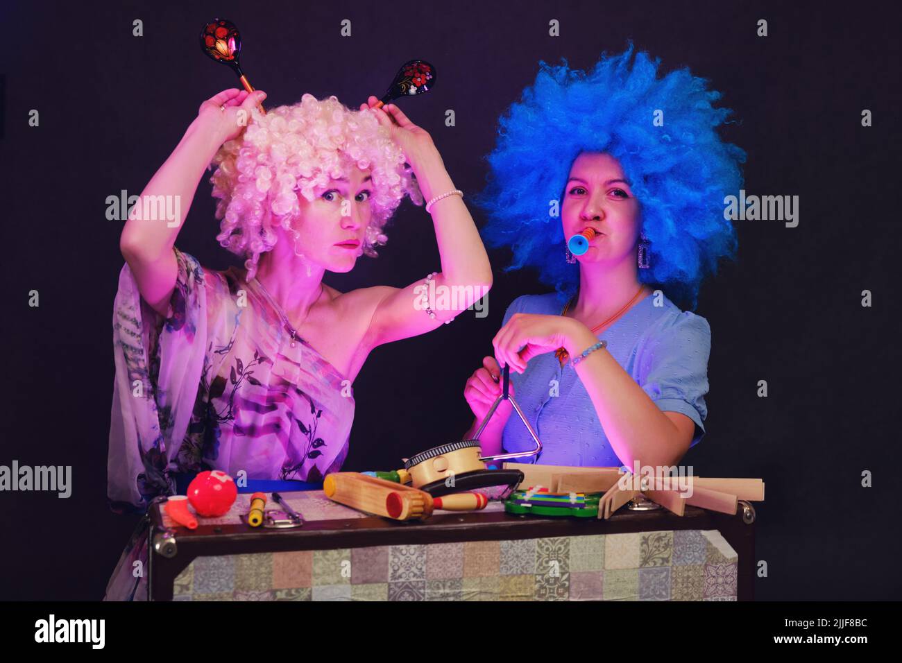 Happy women in funny wigs give a musical performance on a studio black ...