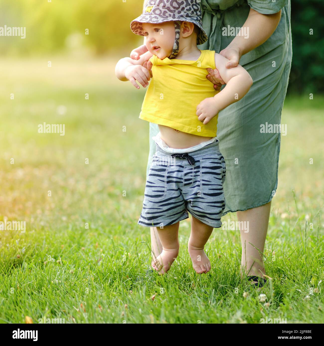Mother teaches to walk happy toddler baby boy in nature on green grass ...