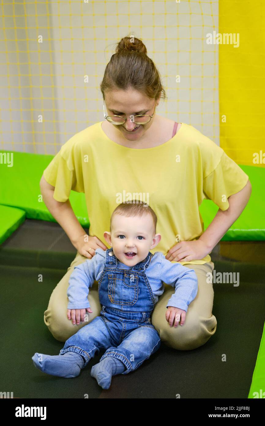Happy toddler baby boy jumps on a trampoline with his mother in the ...