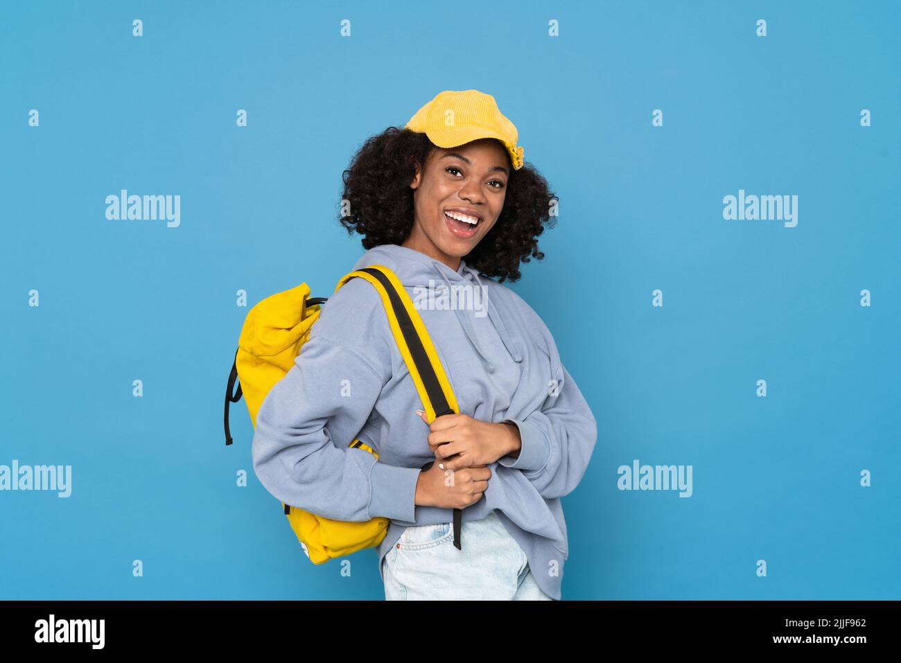 Young black woman smiling while posing with backpack isolated over blue ...