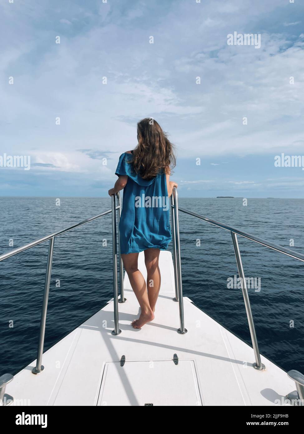 Back view of young woman in blue dress standing on a bow of a yacht ...