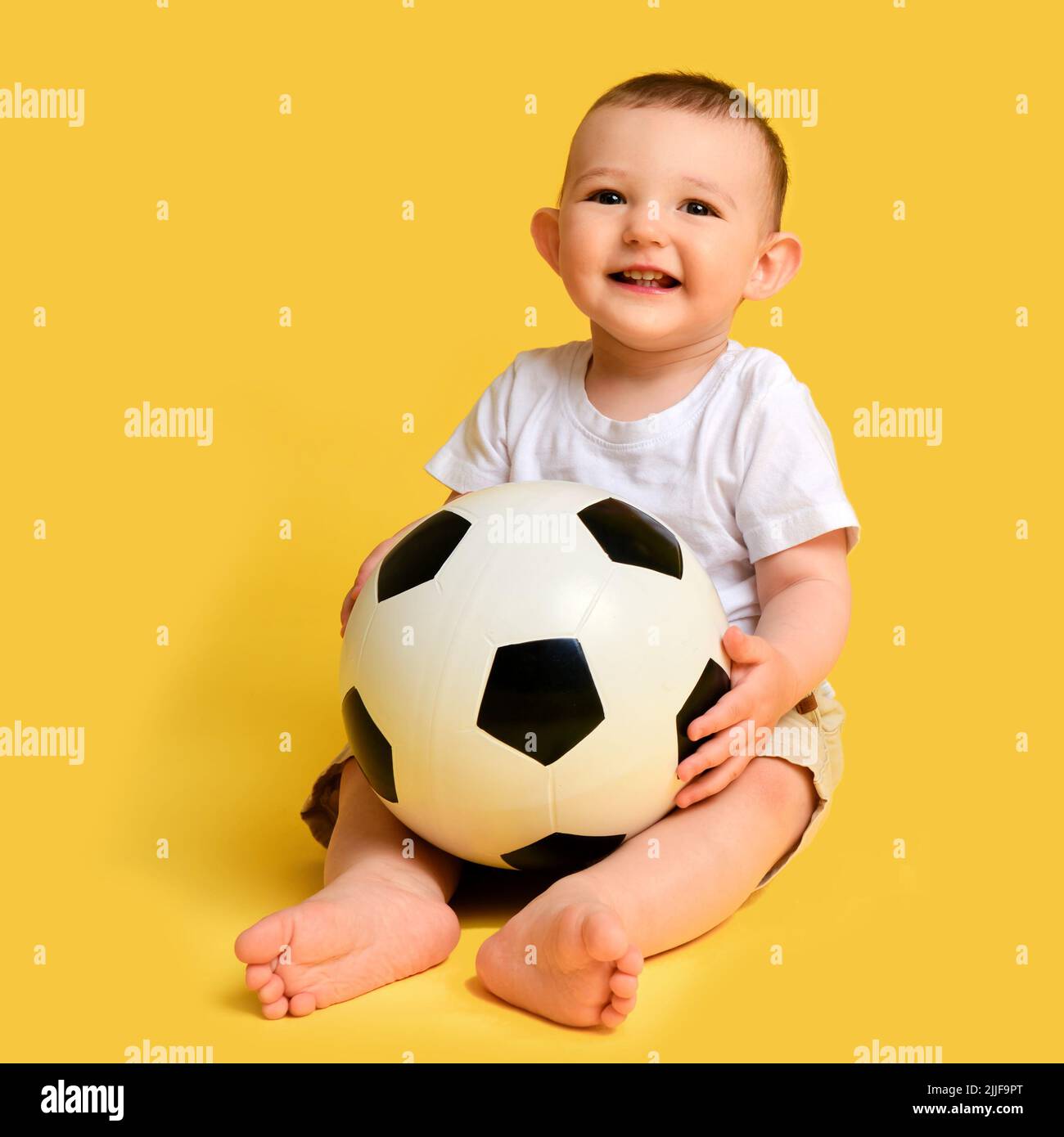 Happy baby boy plays with a soccer ball on a yellow studio background ...