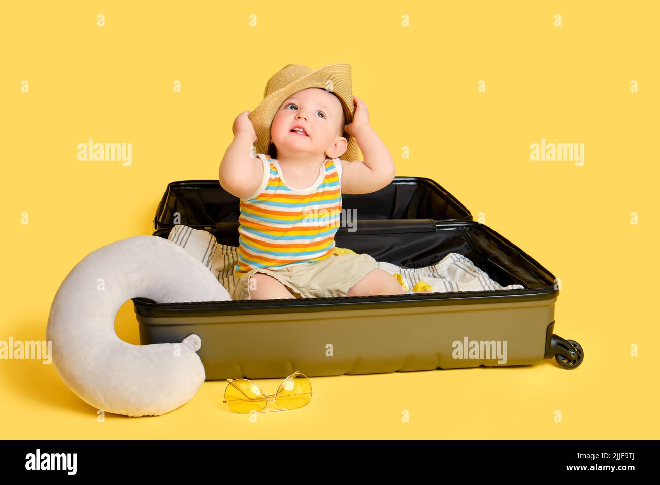 Baby toddler boy sits inside a suitcase with clothes, studio yellow ...