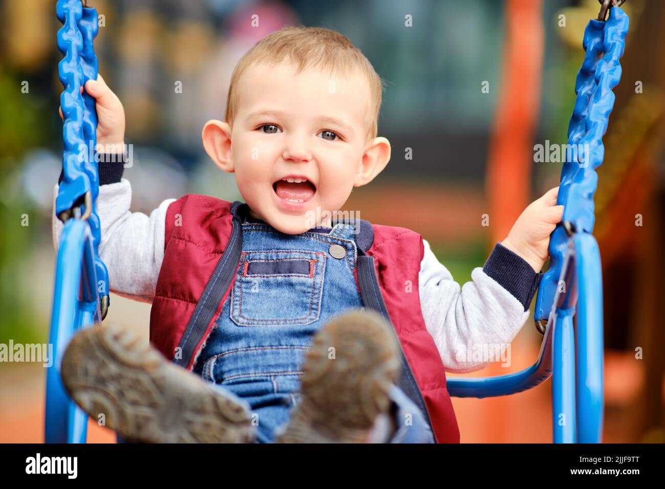 Happy toddler baby boy rides on a swing. Smiling child swinging on the playground, kid aged one ...