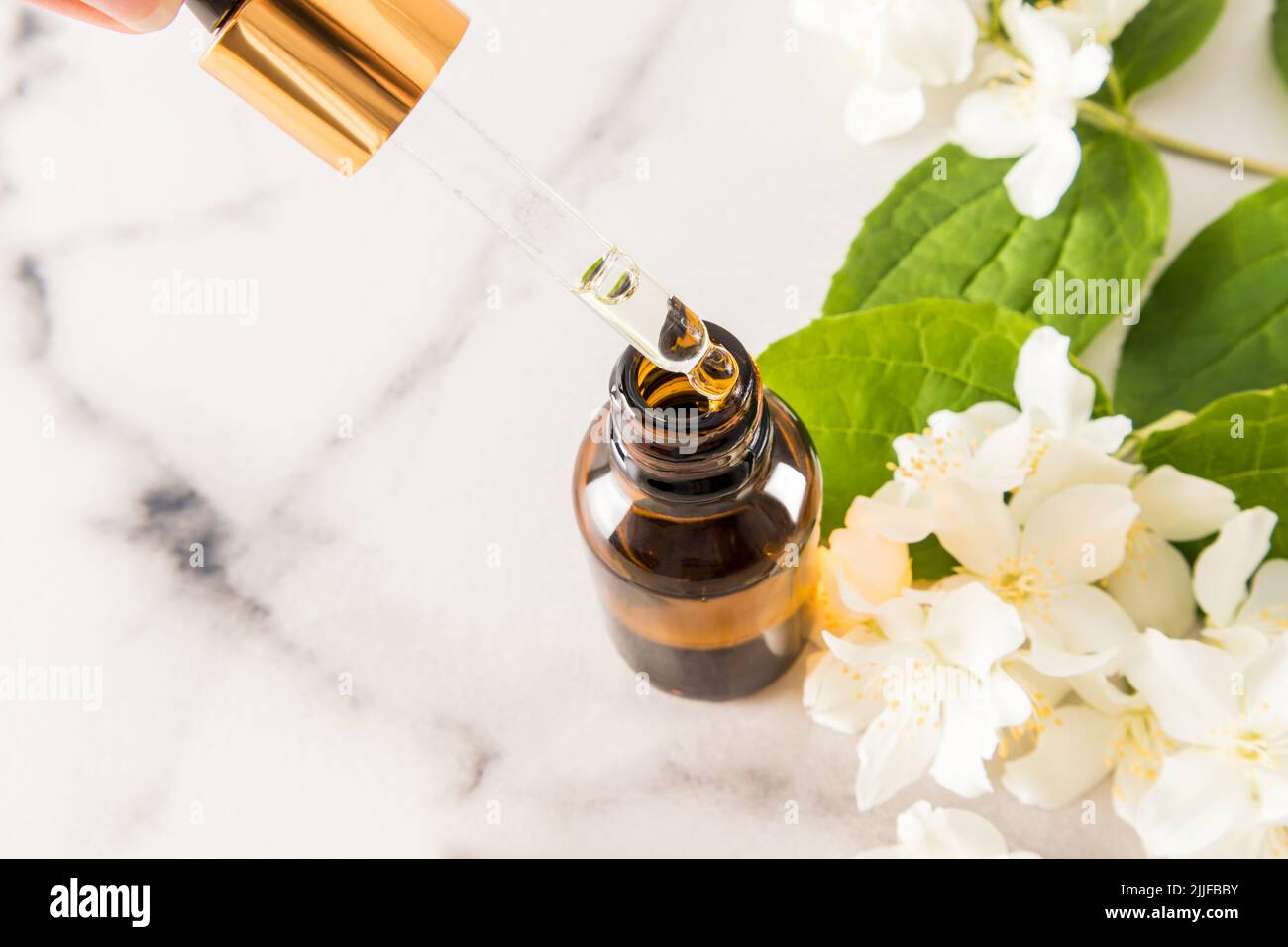 the fingers of the hand hold a pipette filled with cosmetic oil. marble ...