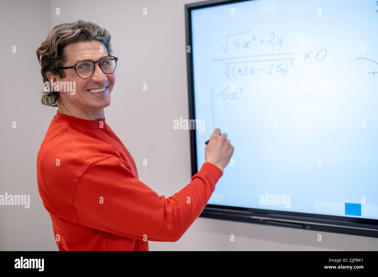 A teacher in red shirt writing on the board at the lesson and looking ...
