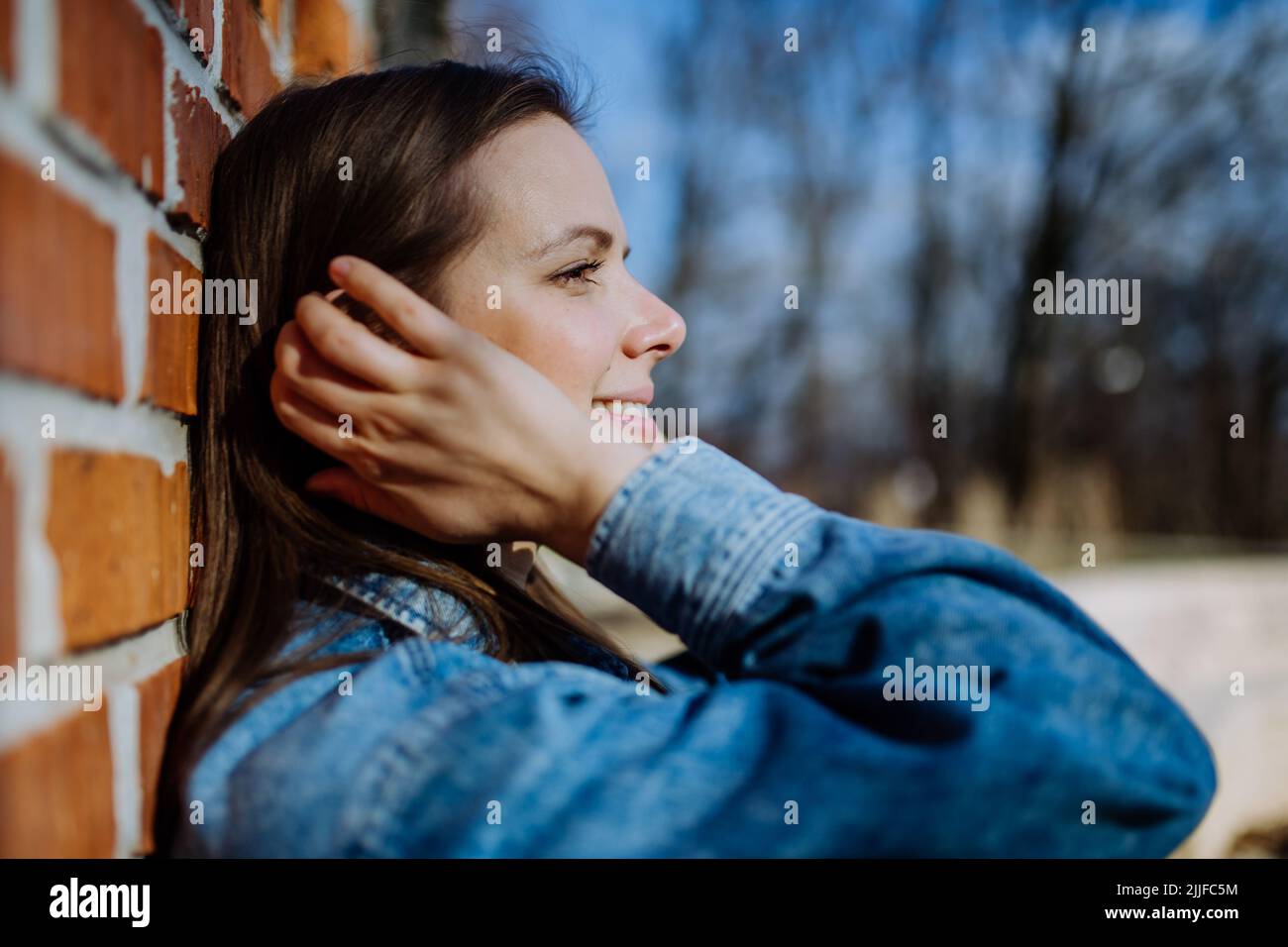 Side view portrait of young woman in denim jacket leaning the brick ...