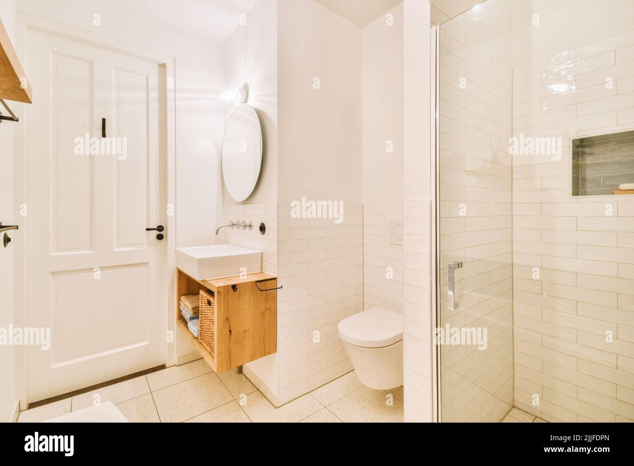 Flush toilet located between sink and shower in small tiled bathroom of ...