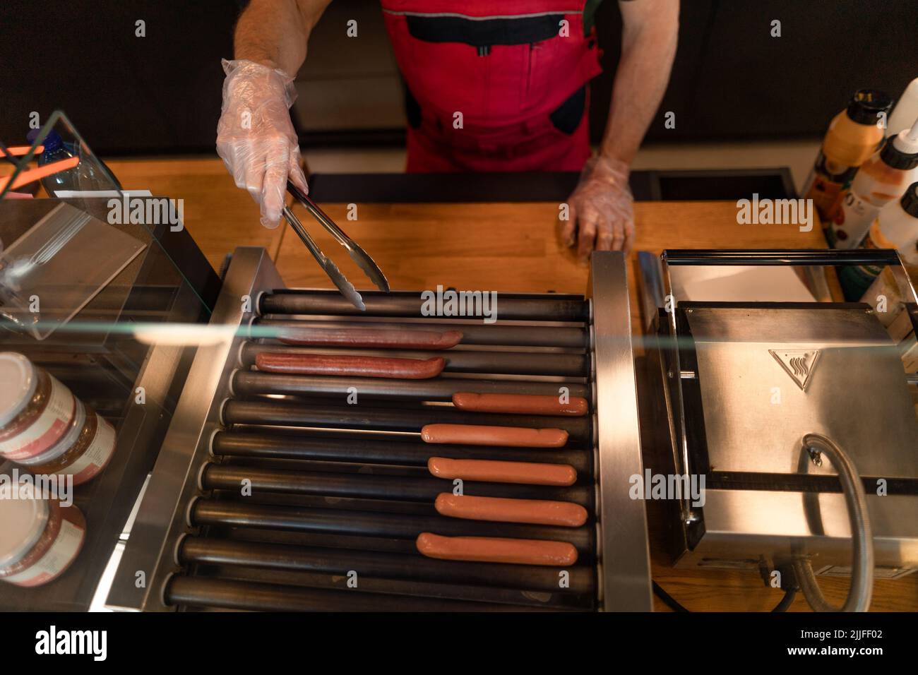 Close-up of waiter standing by counter and prepairing hot-dog to a ...